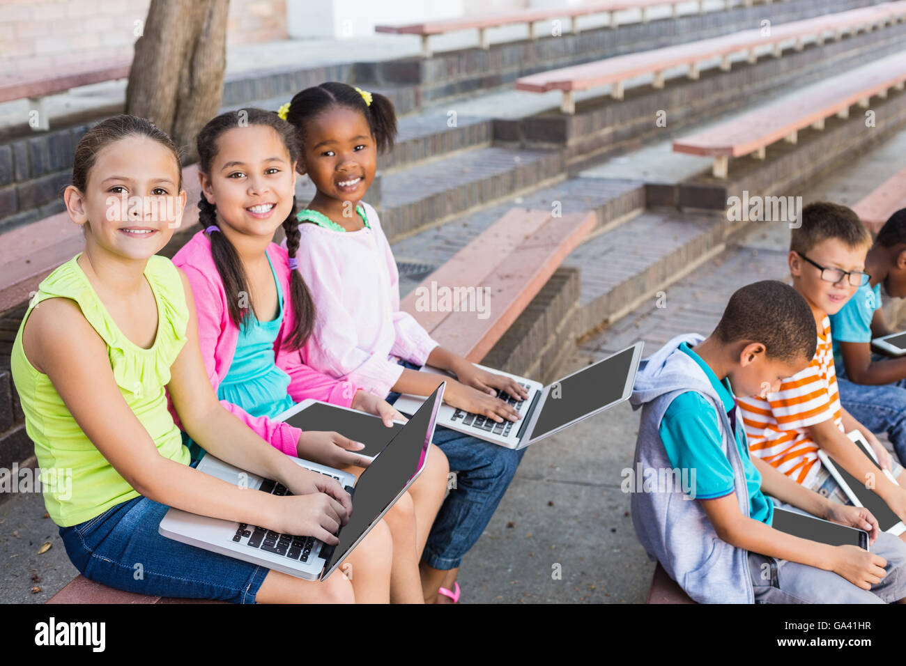 Kids sitting on bench and using laptop Stock Photo - Alamy