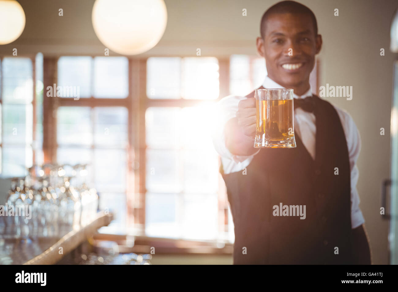 Smiling bartender offering a glass of beer at bar counter Stock Photo ...