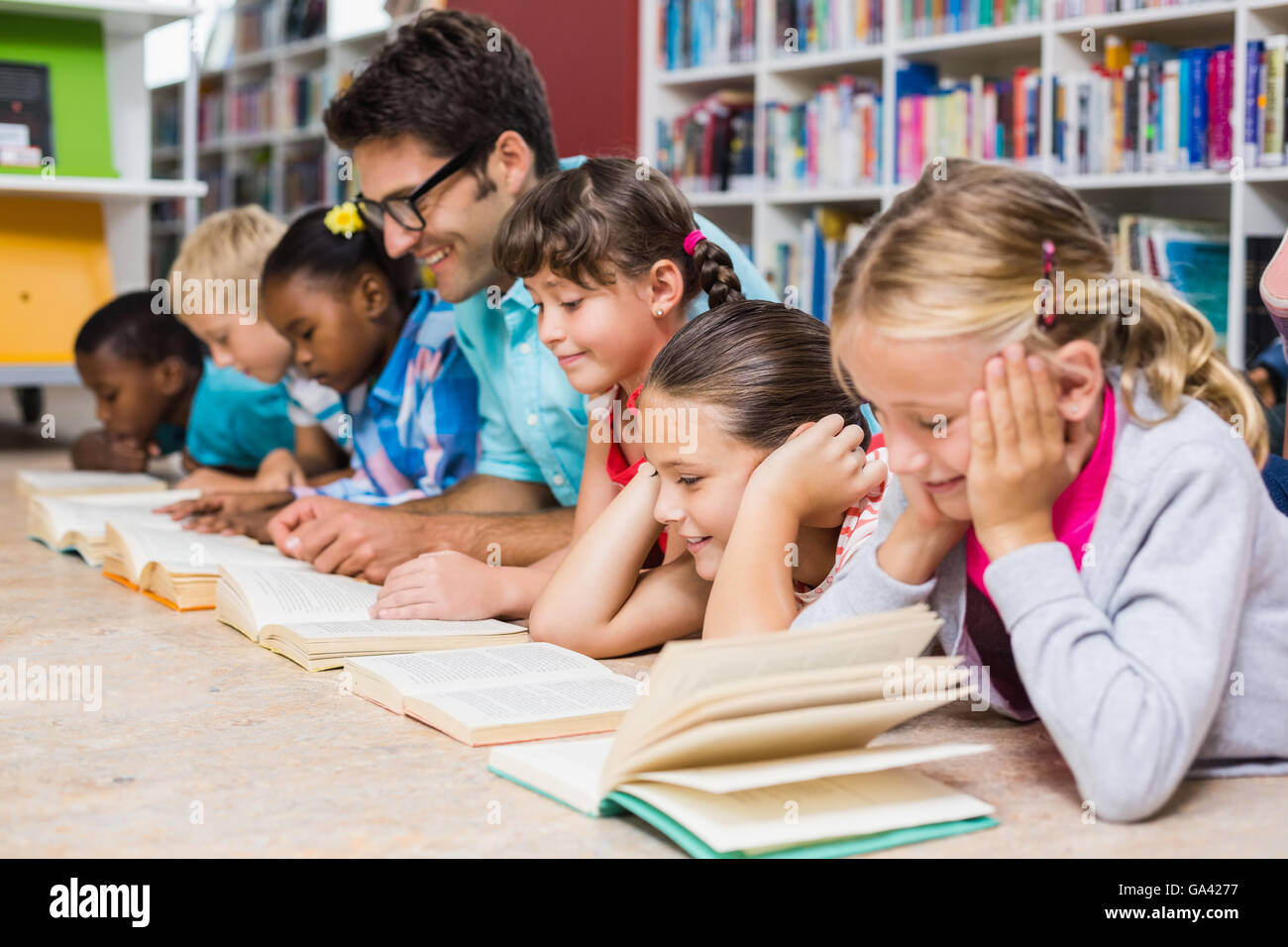 Teacher and kids reading book in library Stock Photo - Alamy