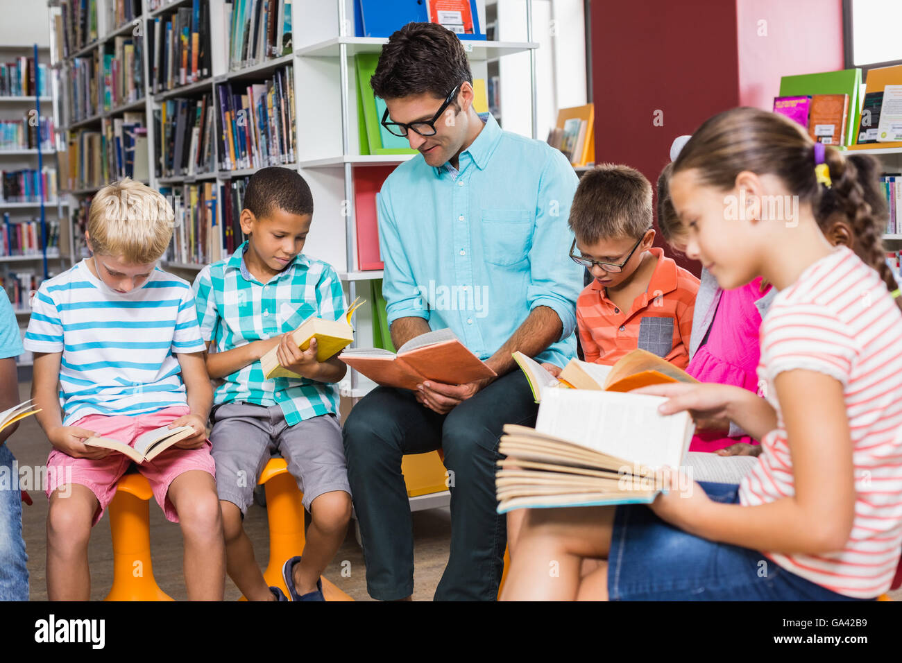 Teacher and kids reading book in library Stock Photo - Alamy