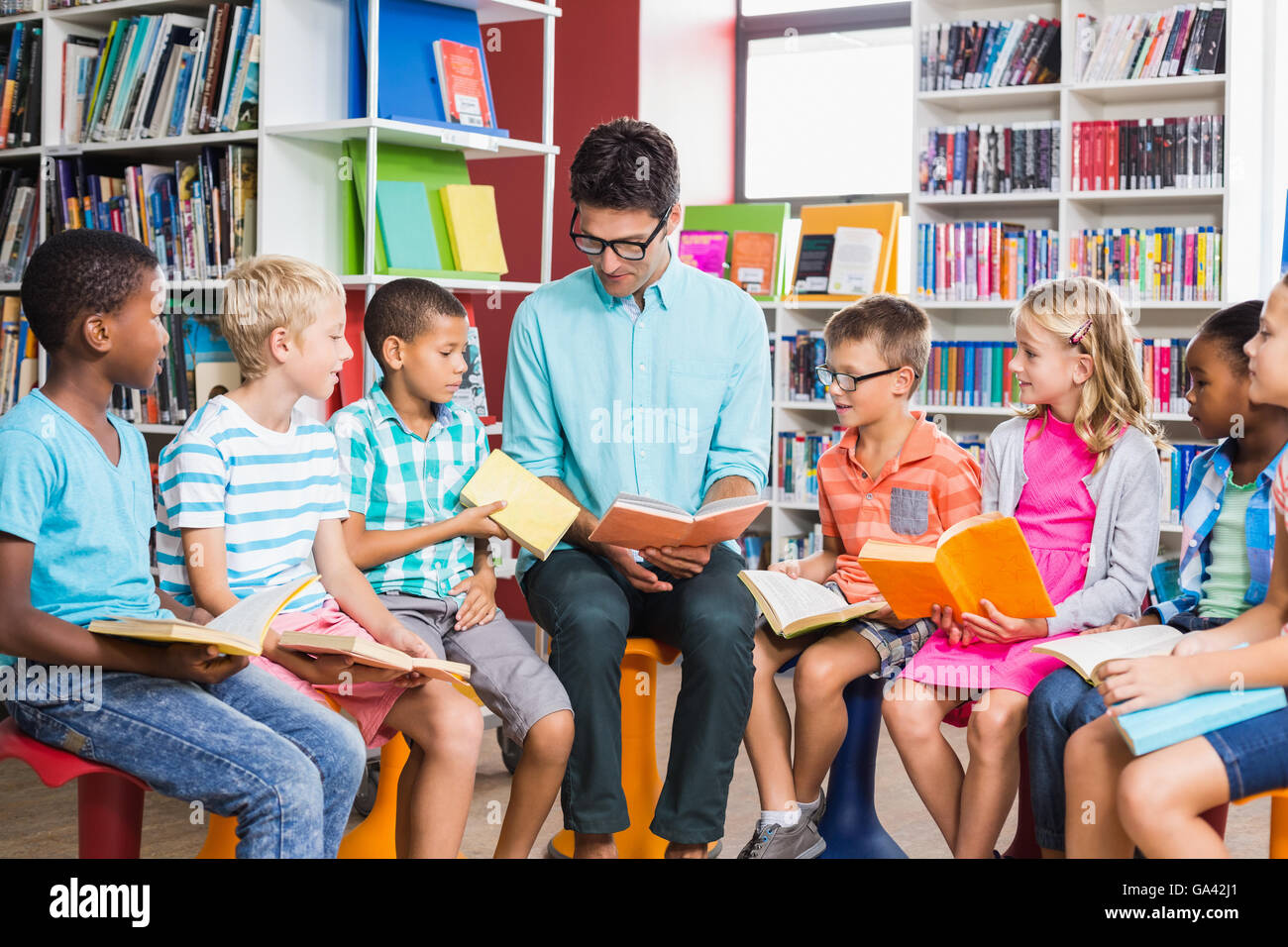 Teacher and kids reading book in library Stock Photo - Alamy