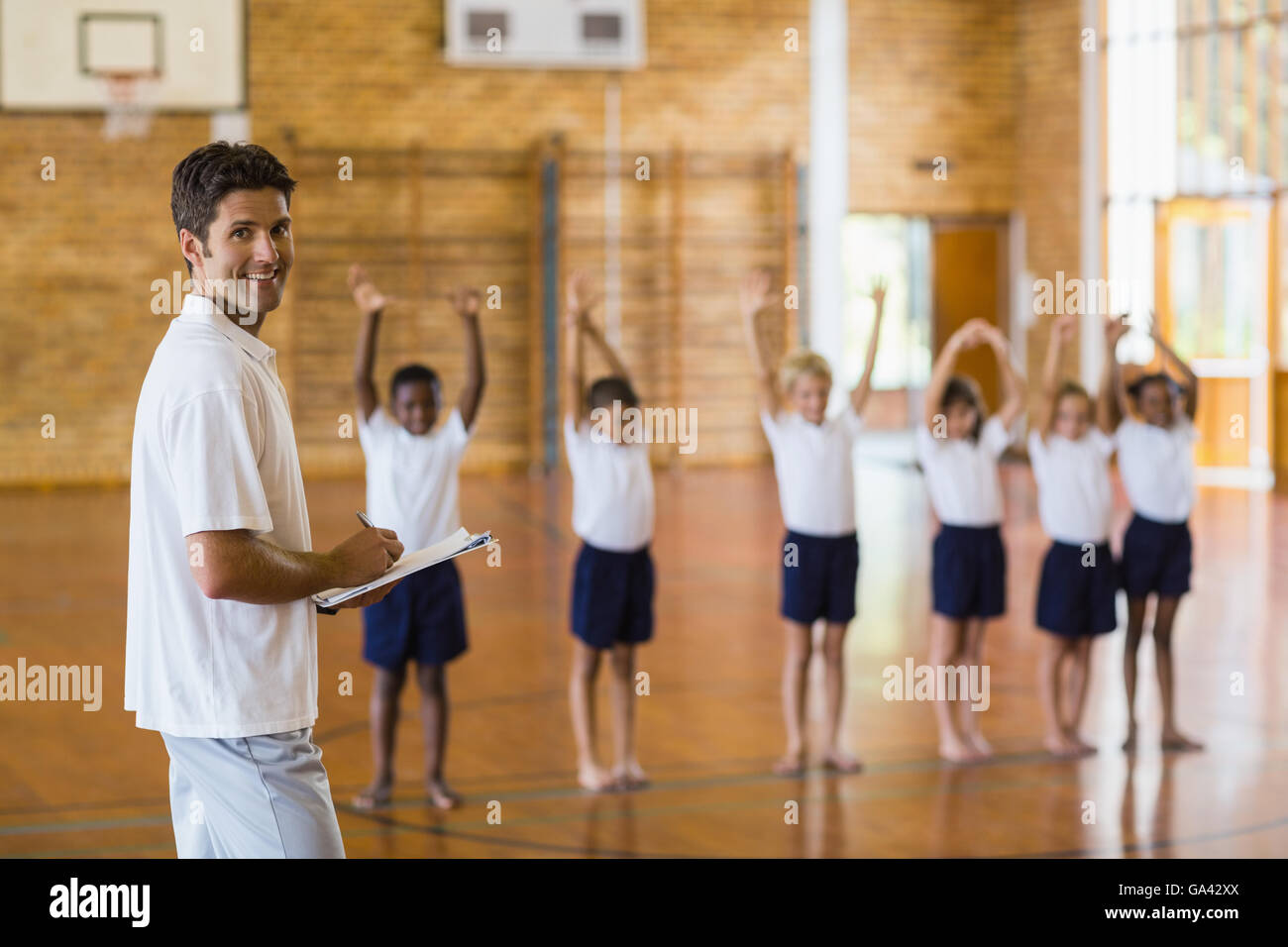 Sports teacher writing notes on clipboard while students exercising ...