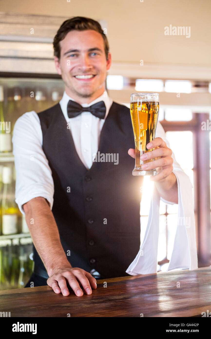 Smiling bartender offering a glass of beer at bar counter Stock Photo ...