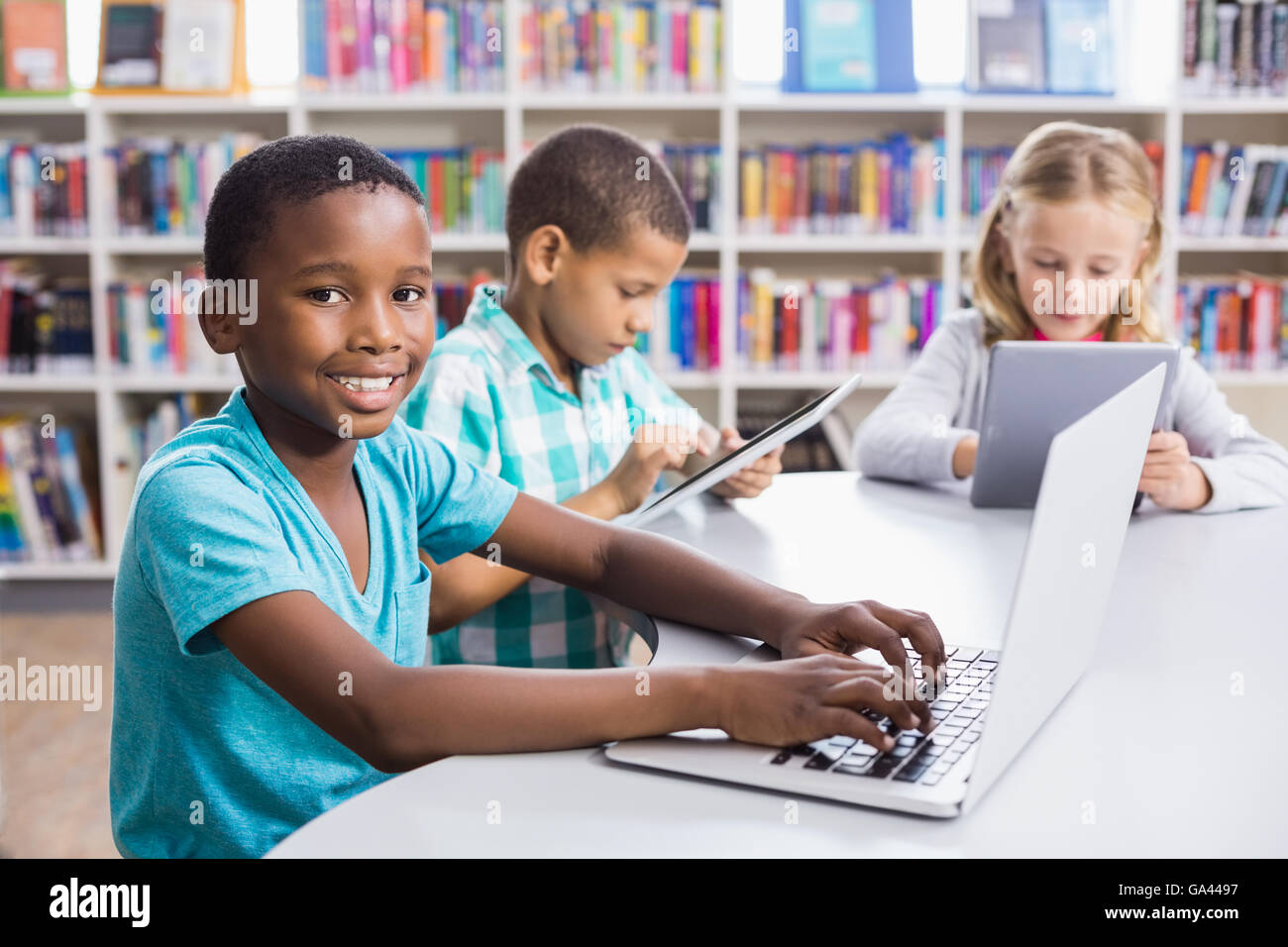 Kids using laptop and digital tablet in library Stock Photo - Alamy