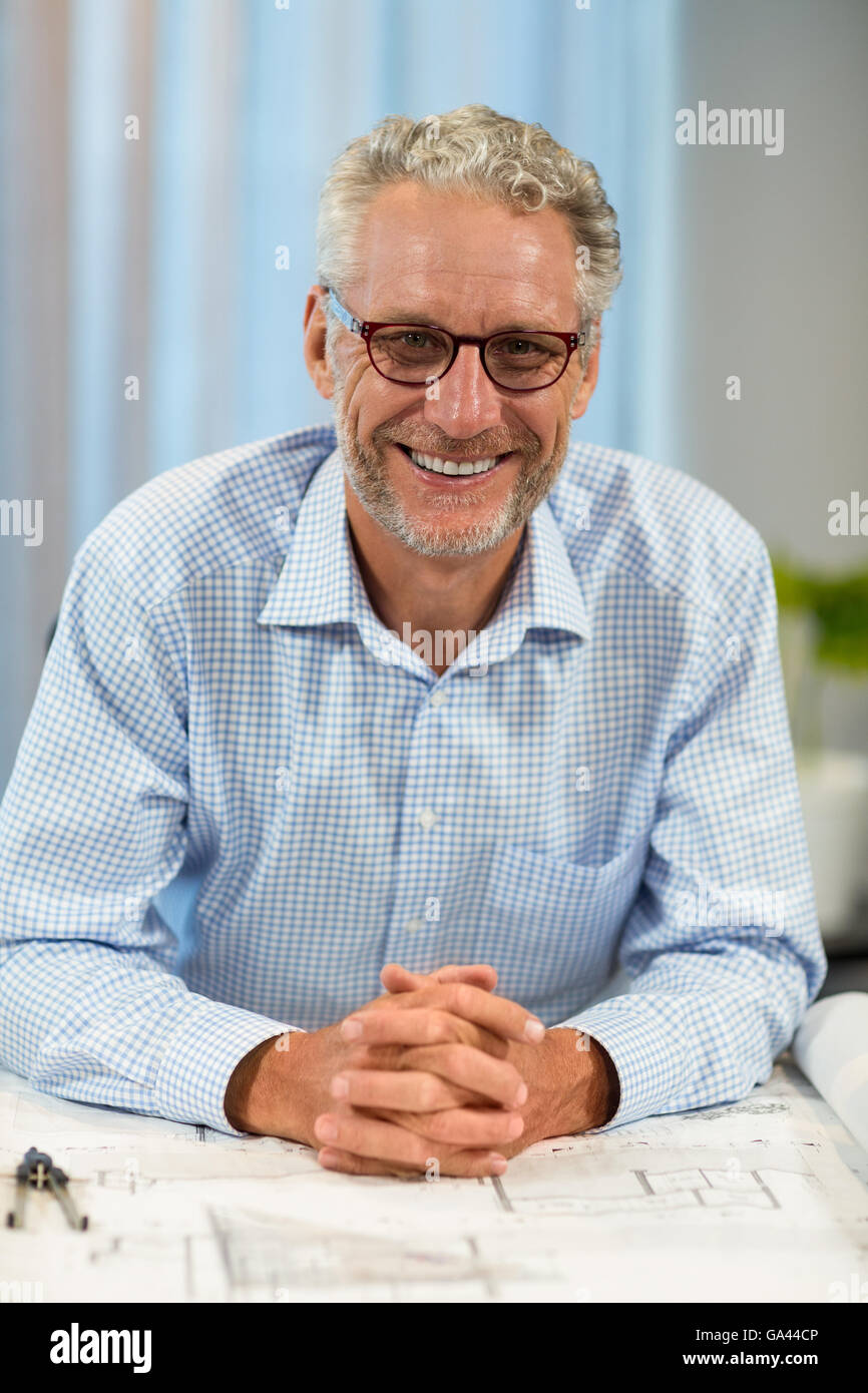 Portrait of smiling businessman with blueprint on desk Stock Photo - Alamy