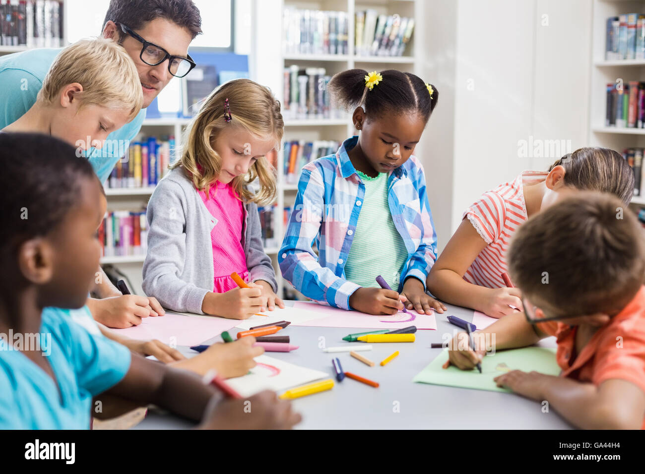 Teacher helping kids with their homework in library Stock Photo - Alamy