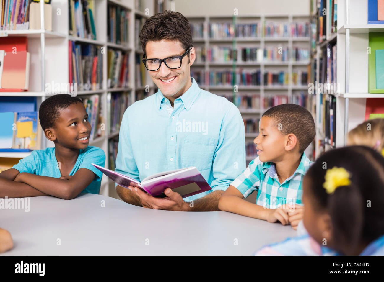 Teacher and kids reading book in library Stock Photo - Alamy