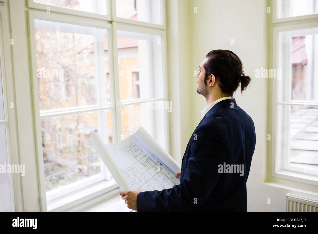 Interior designer with blueprint looking though window Stock Photo - Alamy