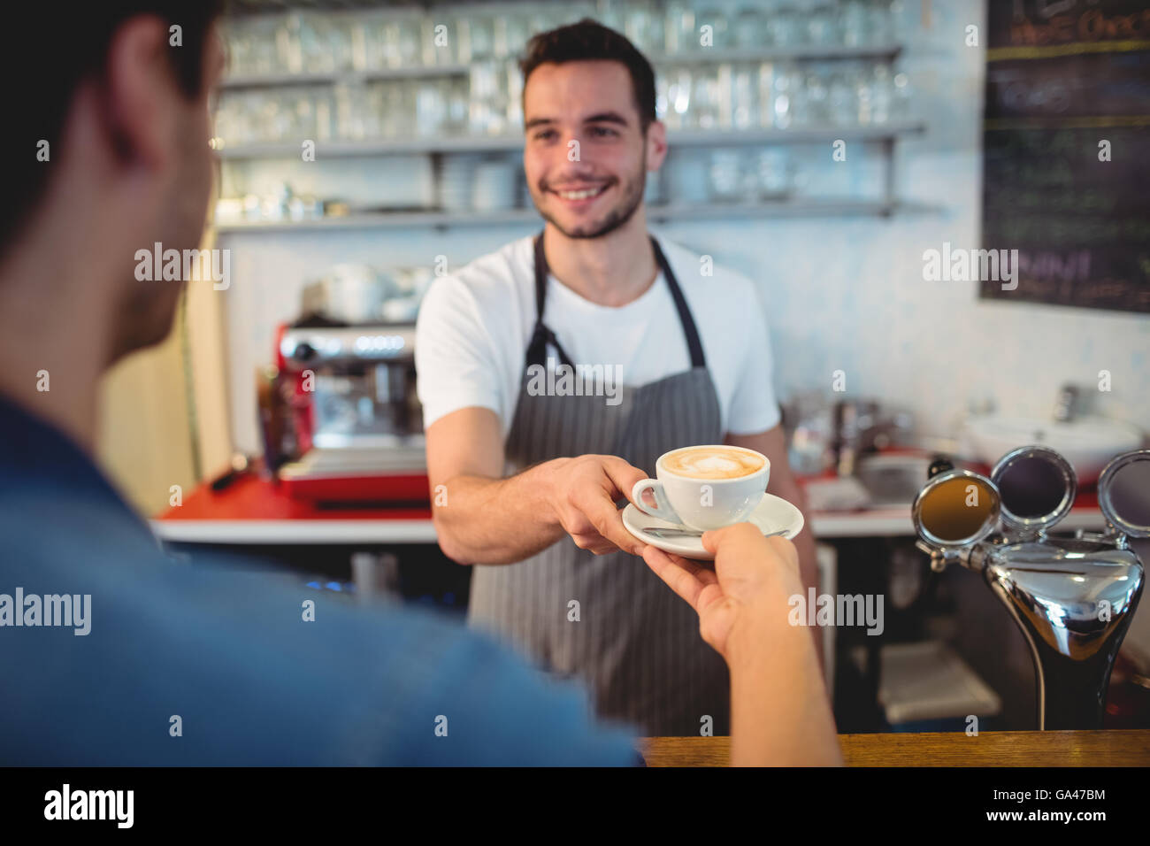 Handsome waiter serving coffee to male customer at cafeteria Stock ...