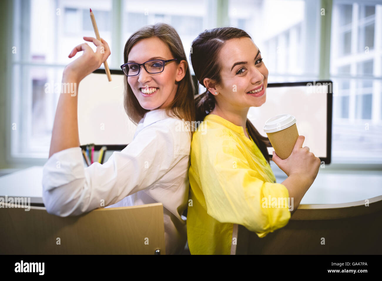 Portrait of happy colleagues sitting back to back at office Stock Photo ...
