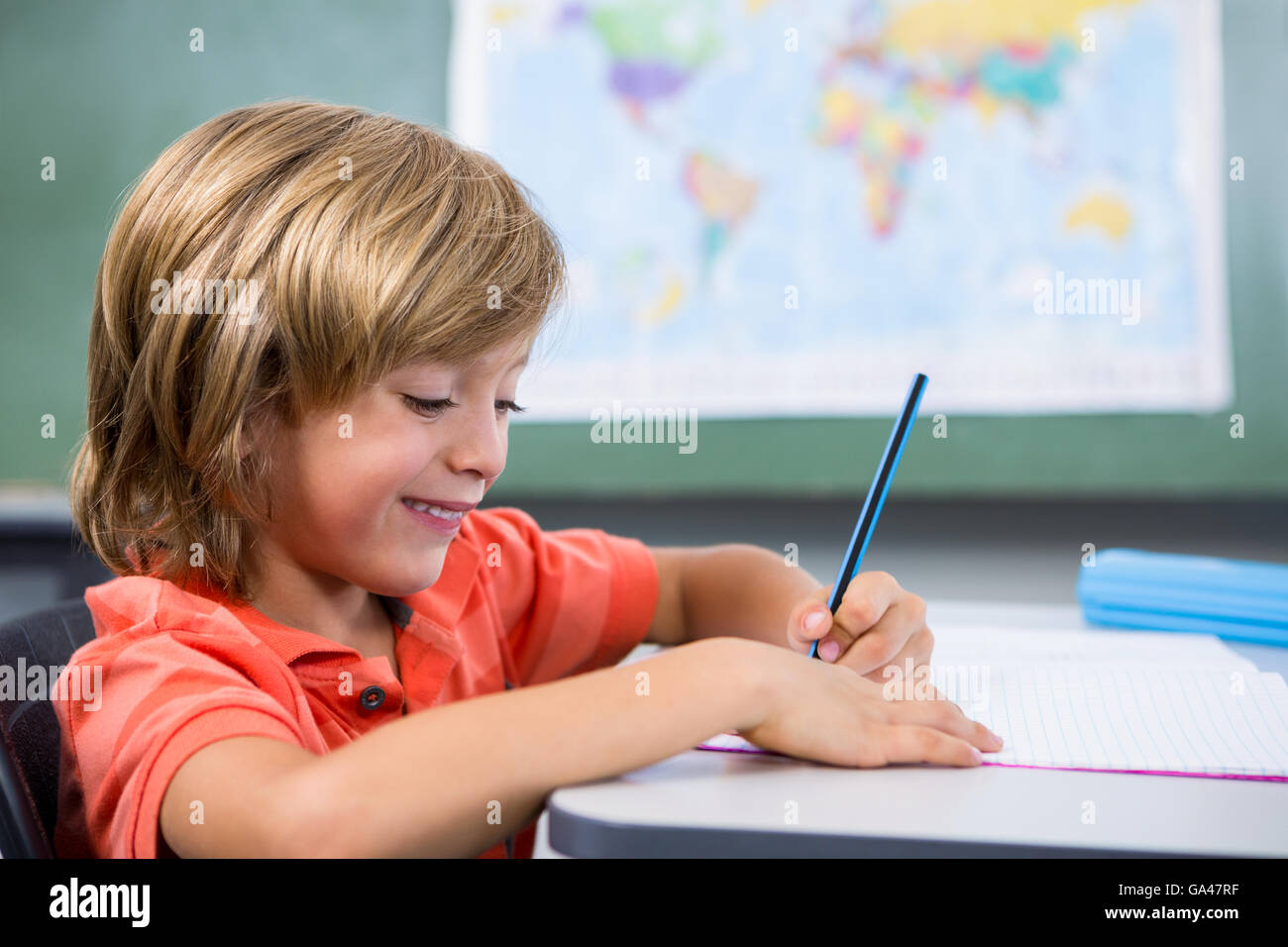 Smiling boy writing on book in classroom Stock Photo - Alamy