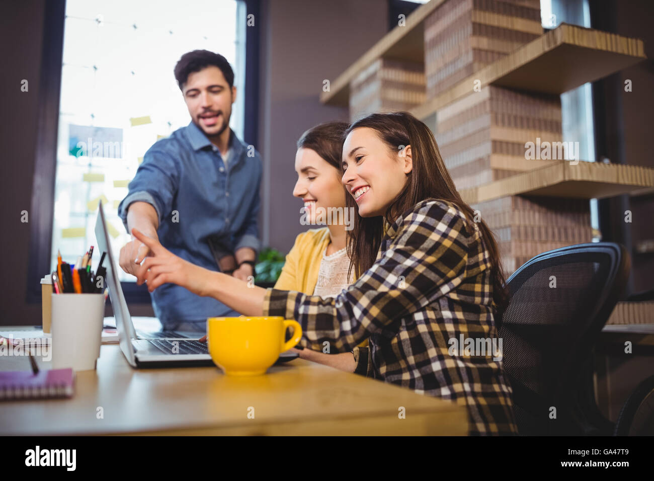 Coworkers smiling while pointing at laptop on desk Stock Photo - Alamy