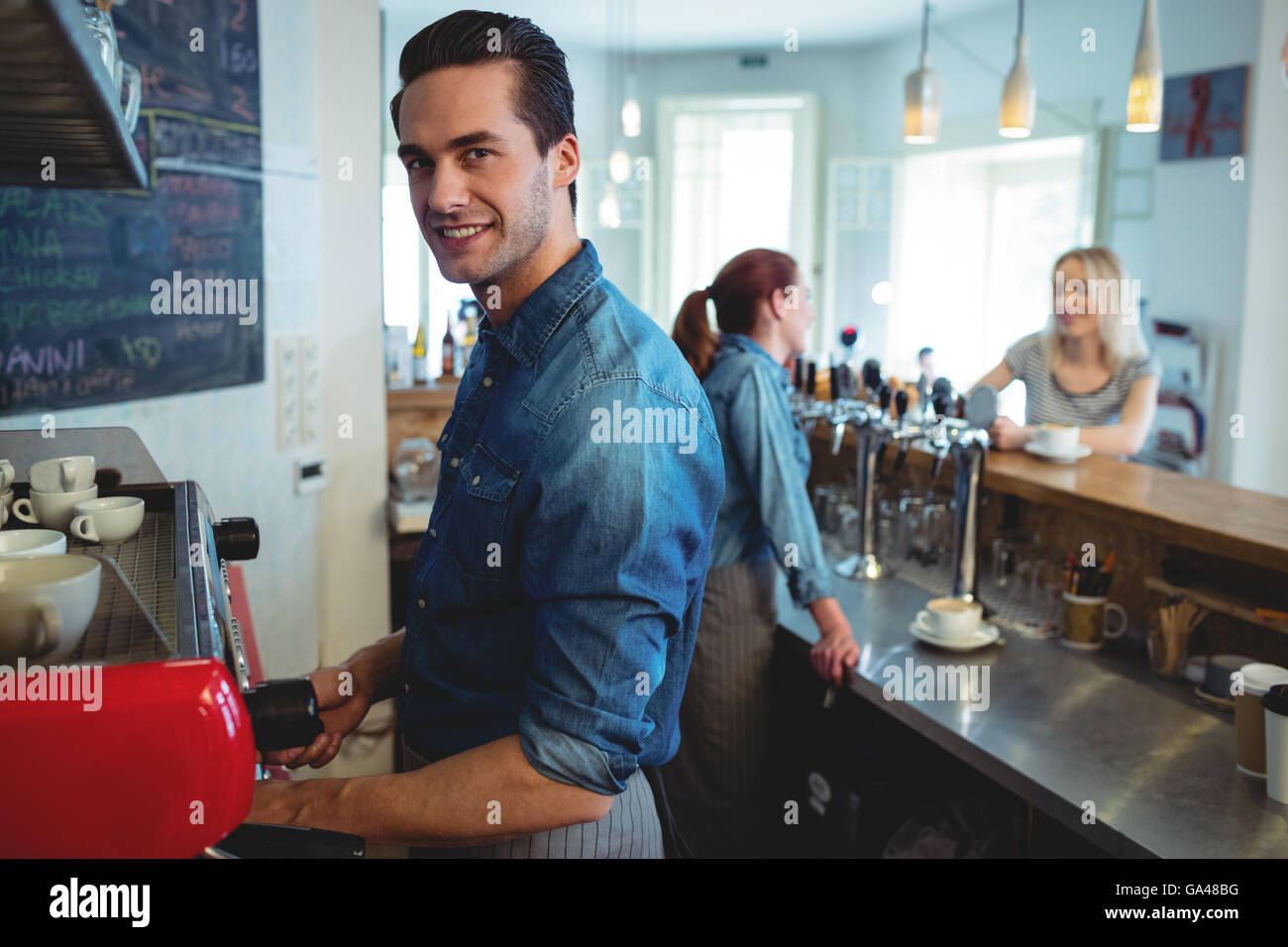 Portrait of barista while colleague talking with customer at cafe Stock ...