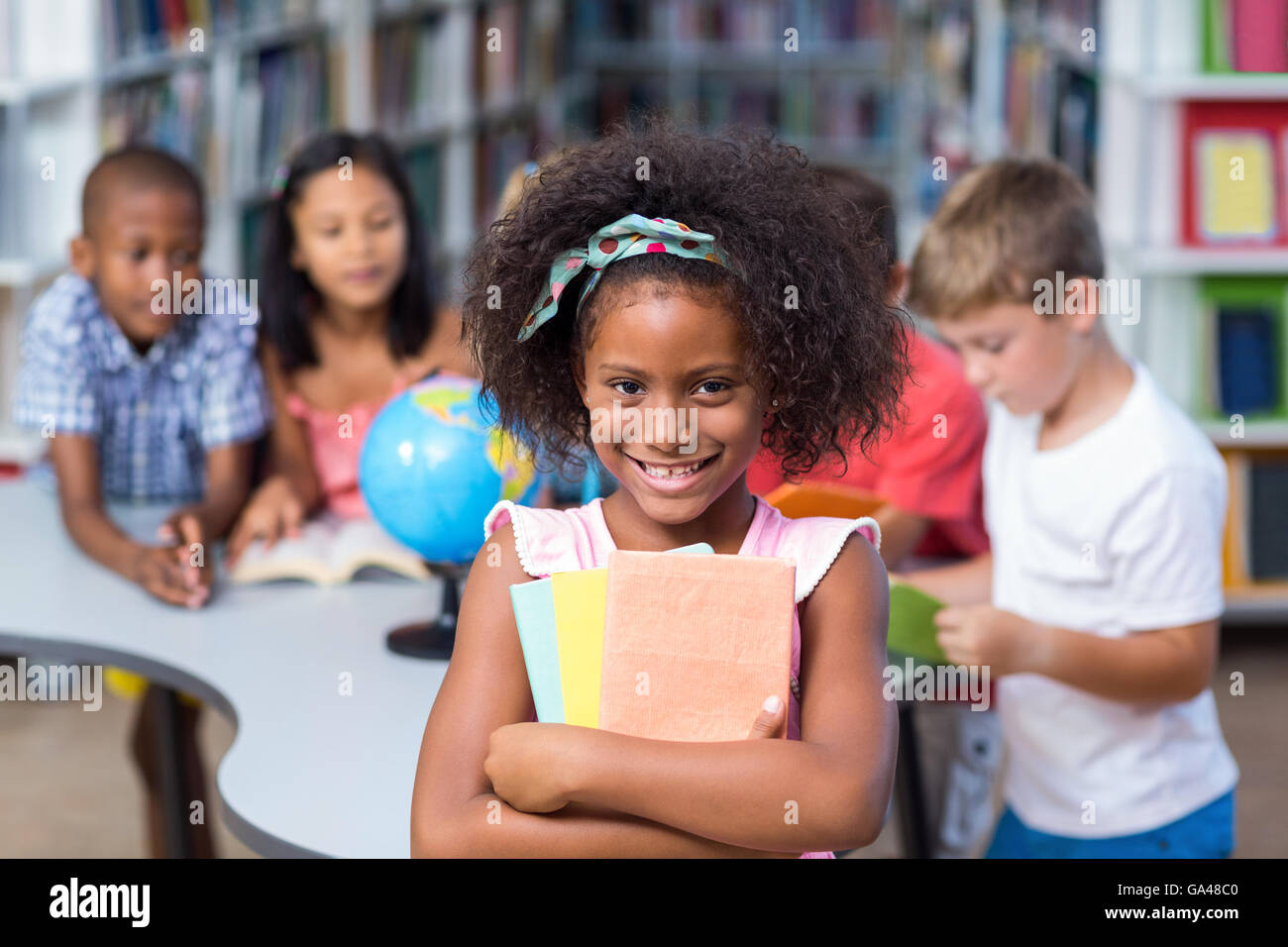 Happy girl holding books against classmates Stock Photo - Alamy