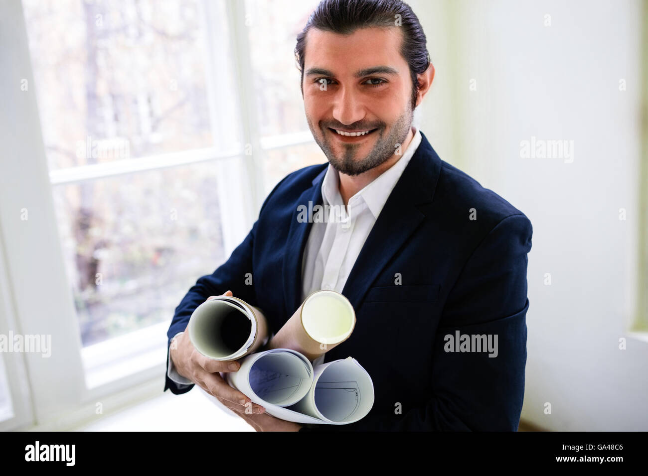 Happy interior designer holding blueprints Stock Photo - Alamy