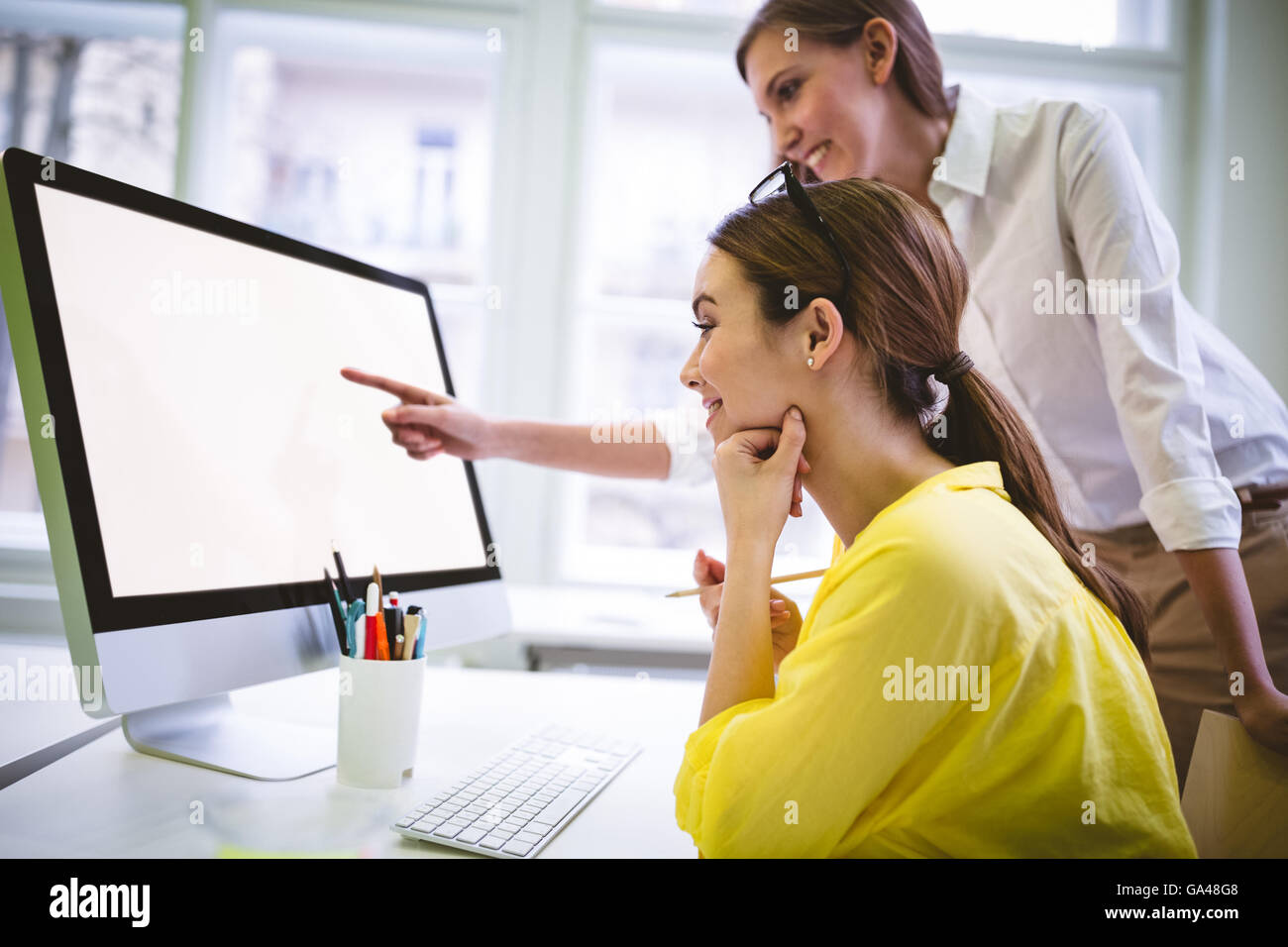 Happy businesswoman pointing at computer screen to colleague at ...