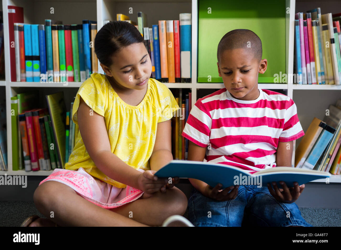 Elementary students reading book at library in school Stock Photo - Alamy