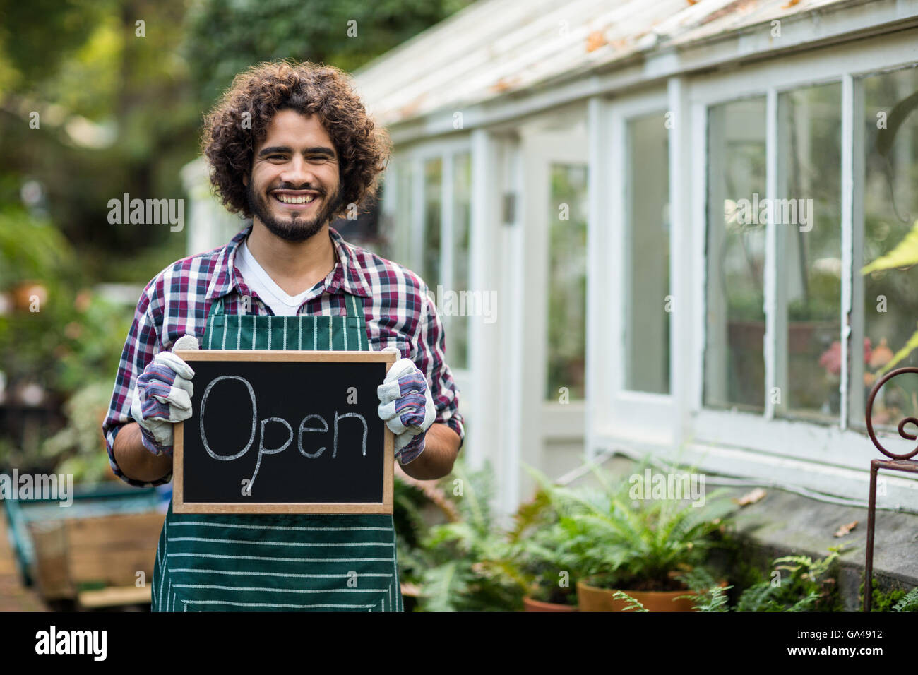 Gardener holding open sign placard outside greenhouse Stock Photo - Alamy