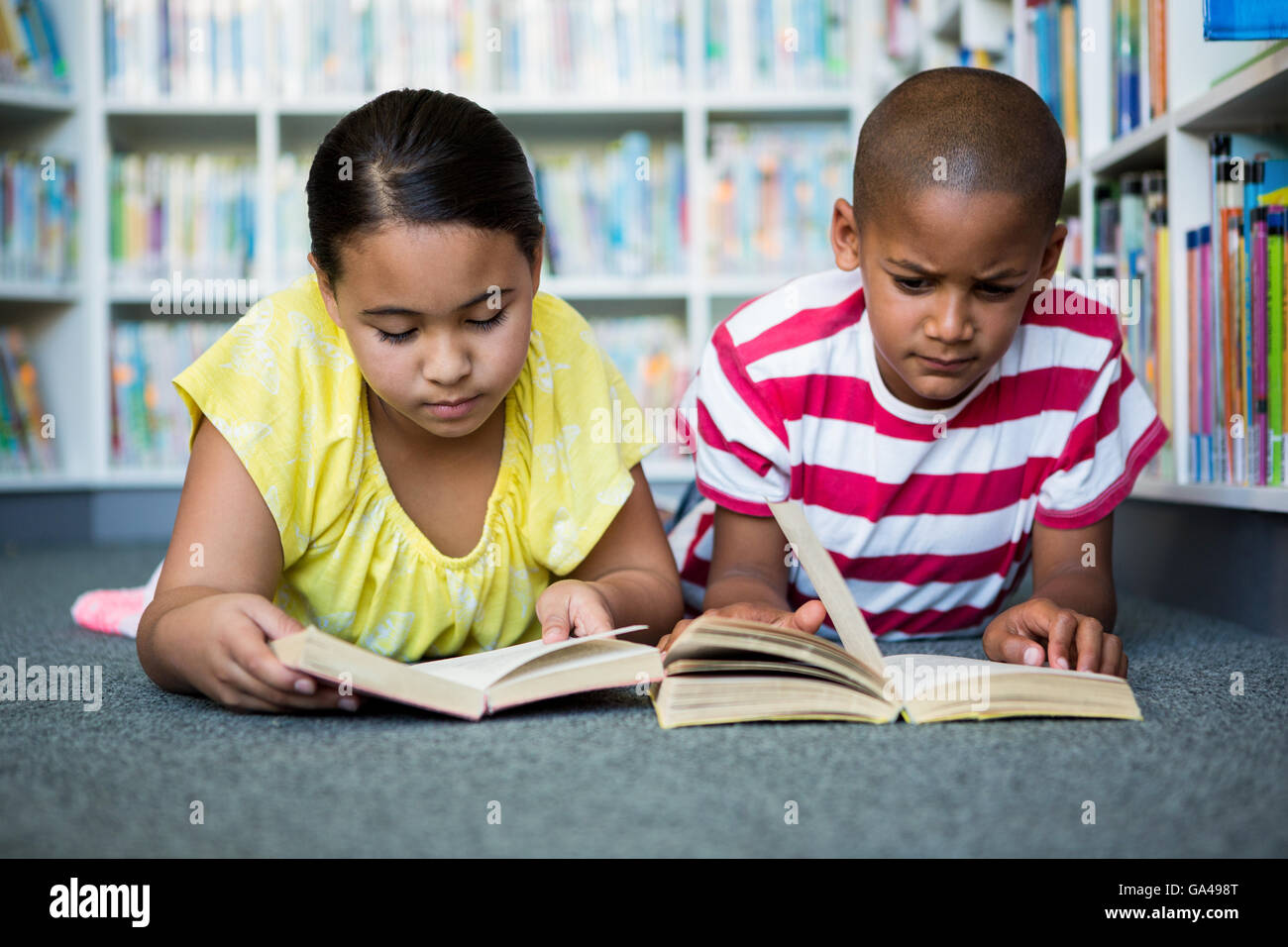 Students reading books while lying at library in school Stock Photo - Alamy