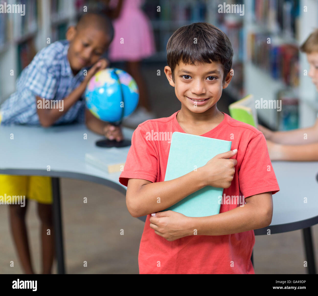 Happy holding books against classmates Stock Photo - Alamy