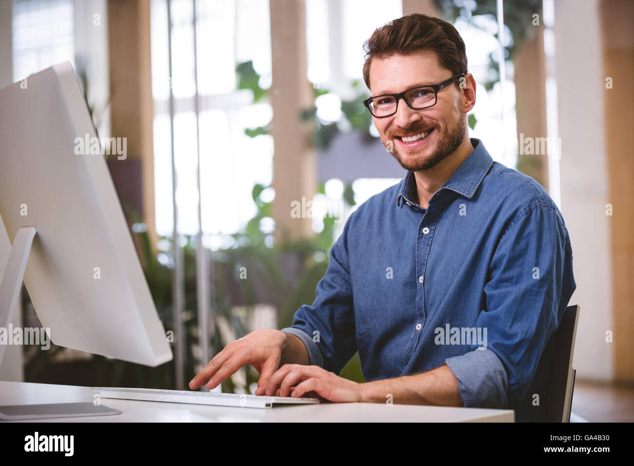Portrait of happy businessman working on computer at creative office ...