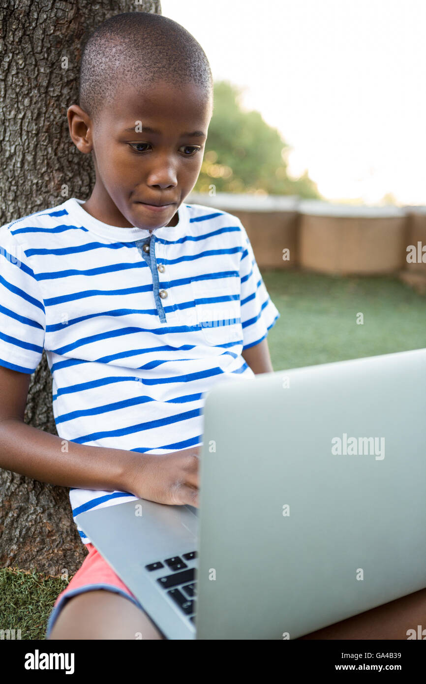 Boy using laptop while sitting by tree Stock Photo - Alamy