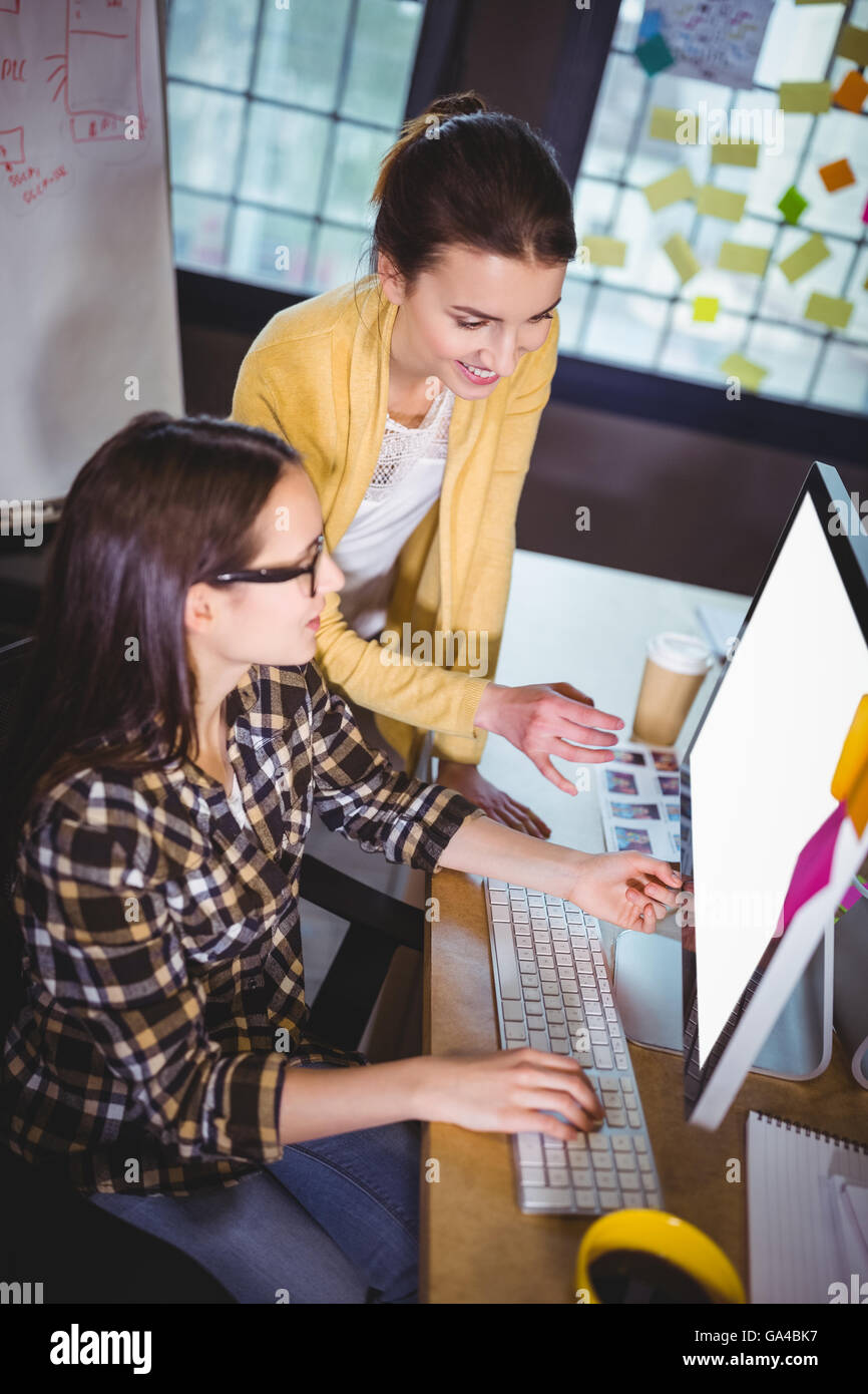Female colleagues smiling while discussing over computer Stock Photo ...