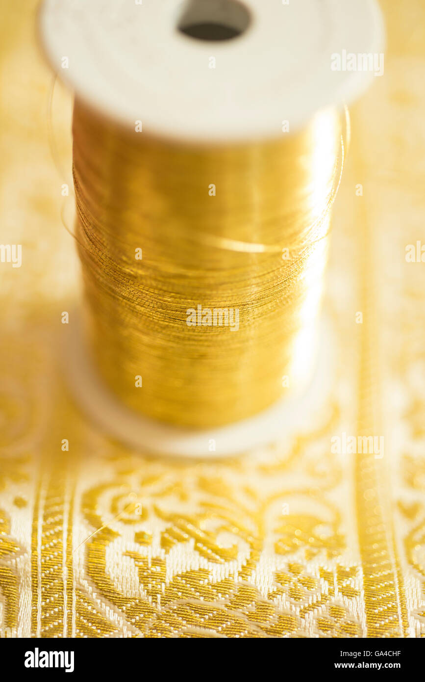 A spool of gold-colored thread on embroidered fabric Stock Photo - Alamy