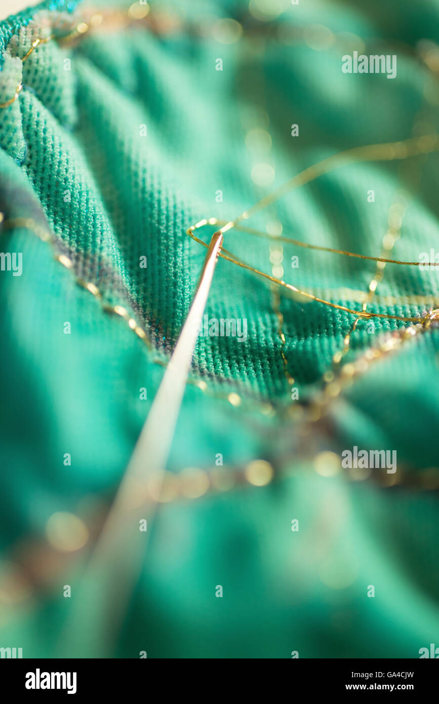 Gold-threaded needle stitching through green cloth Stock Photo - Alamy