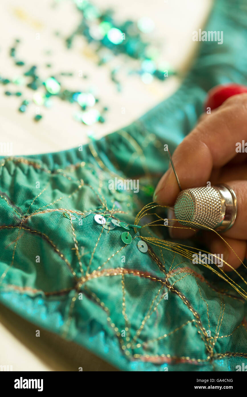 Fingers pulling gold thread through a green sequin on a green garment ...