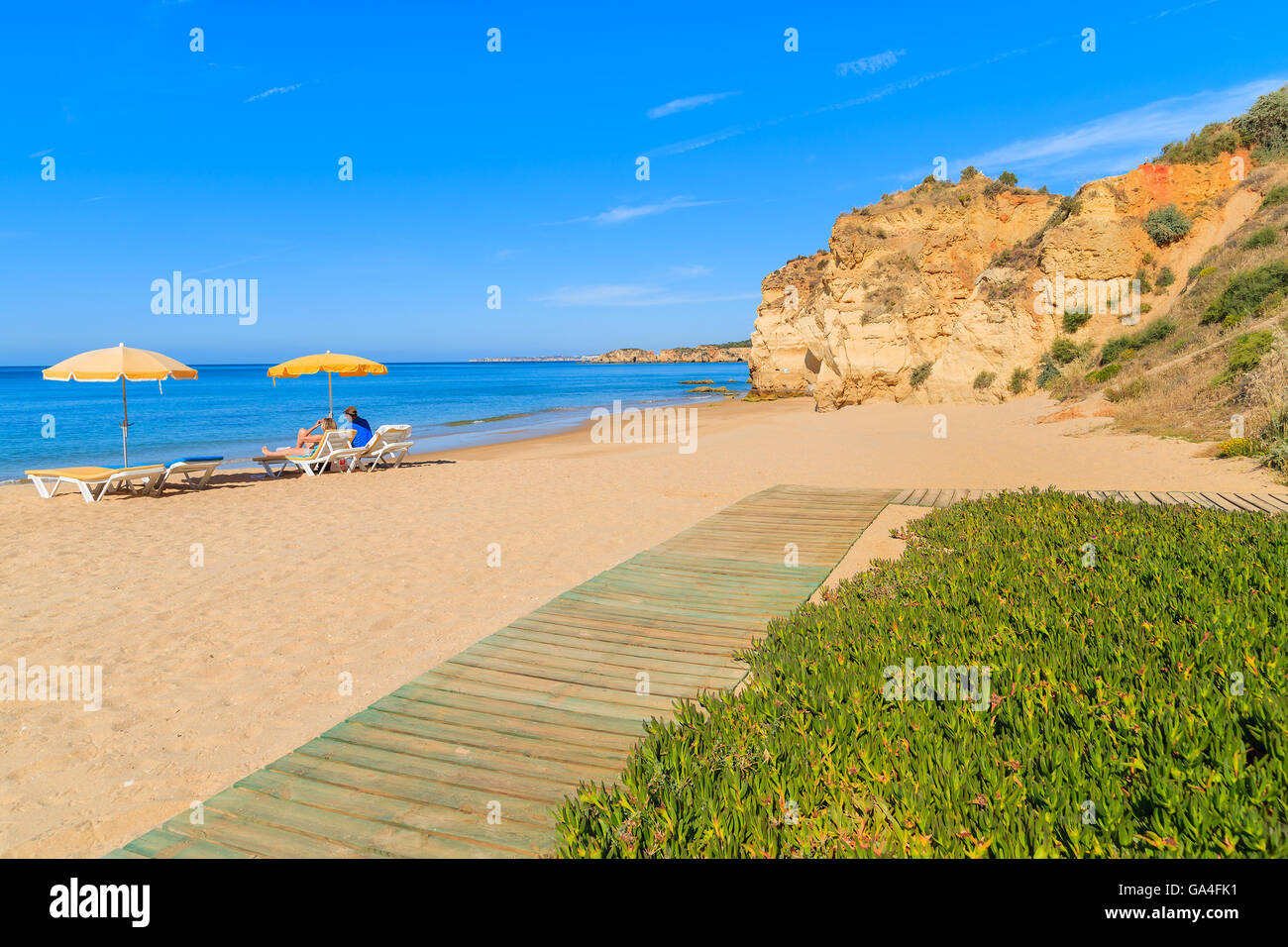 Walkway on sandy beautiful Praia da Rocha beach and two sun umbrellas ...
