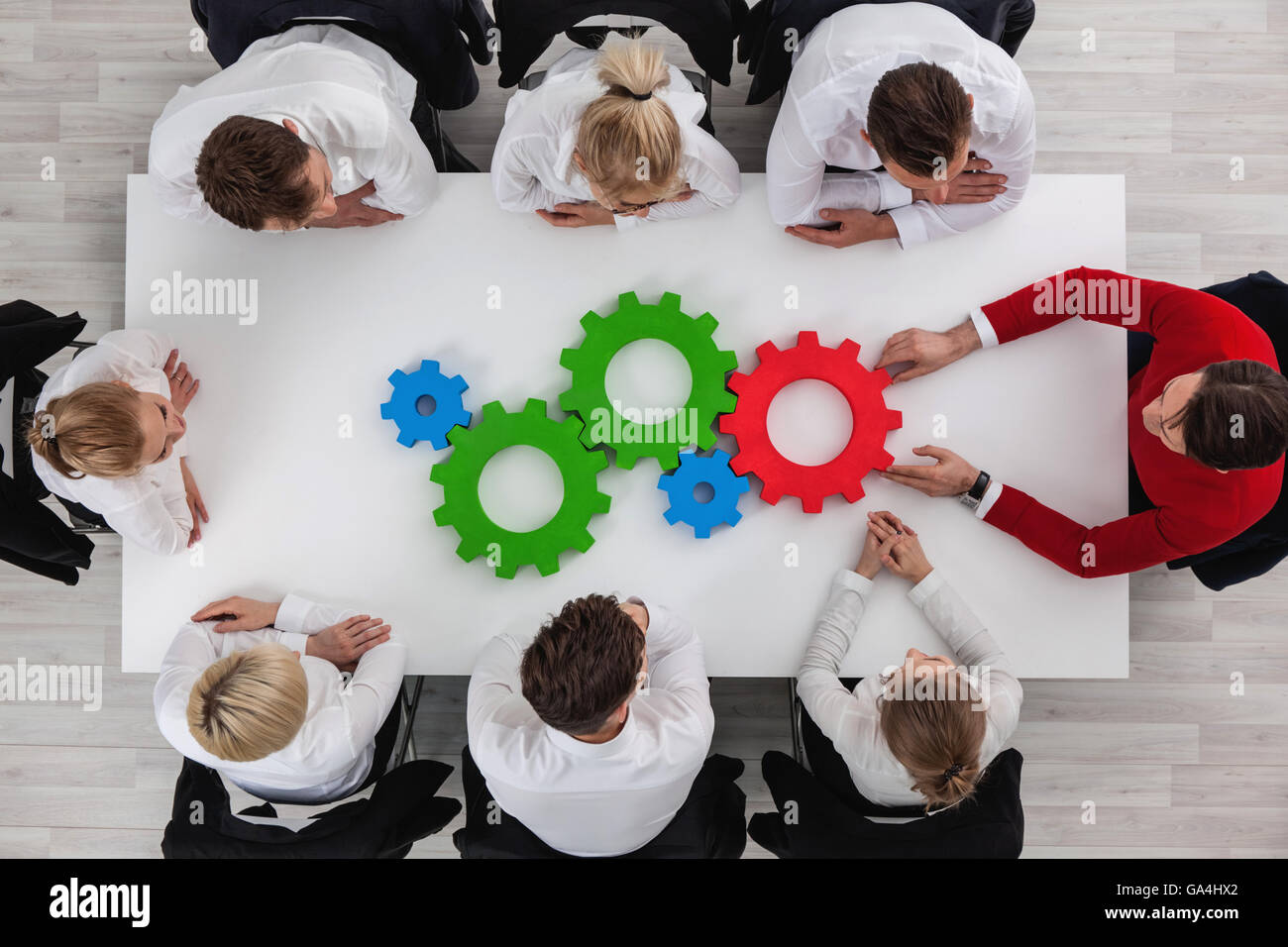 Business team sitting around the table with cogs, teamwork concept ...