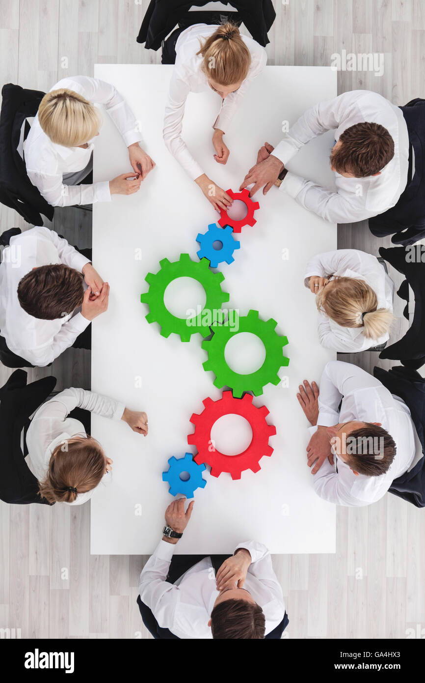 Business team sitting around the table with cogs, teamwork concept ...