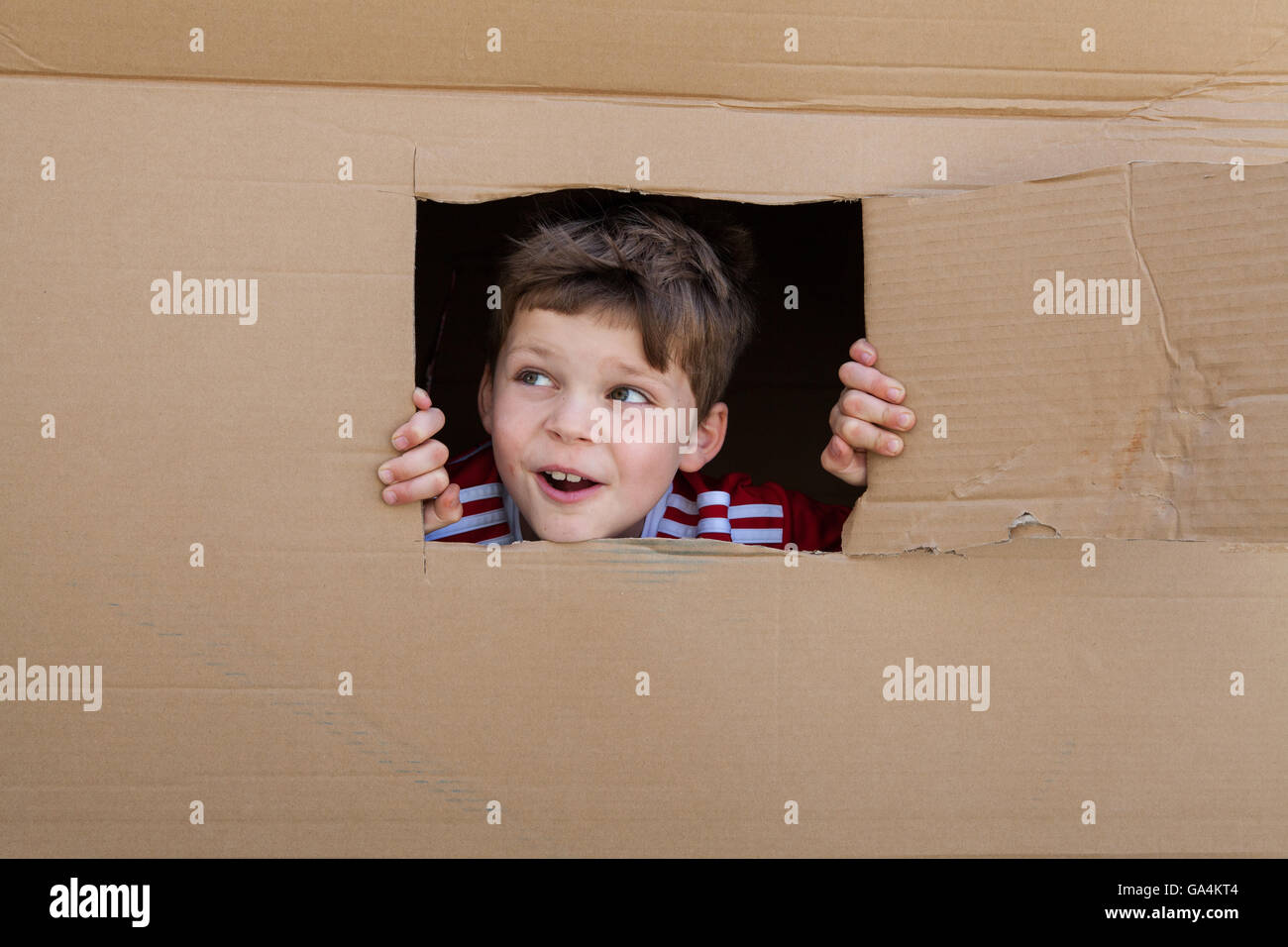 A 7 year old boy looks out of a window cut from a cardboard box Stock ...