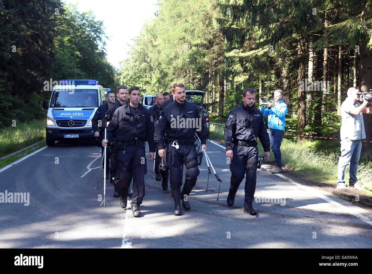 Police officers carrying searching sticks walk along a road between ...