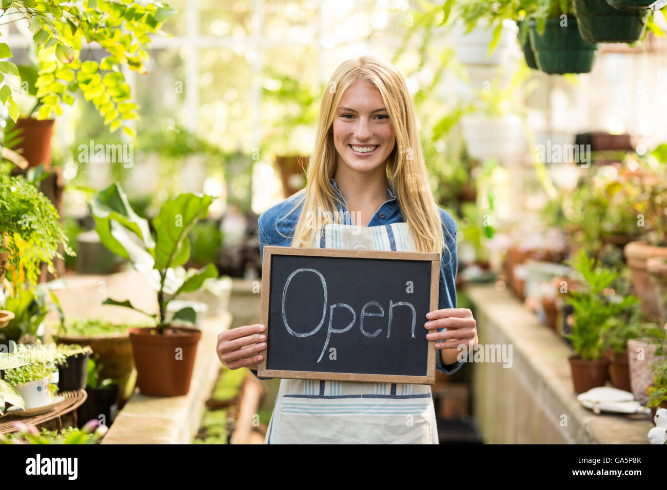 Young woman holding open sign placard at greenhouse Stock Photo - Alamy