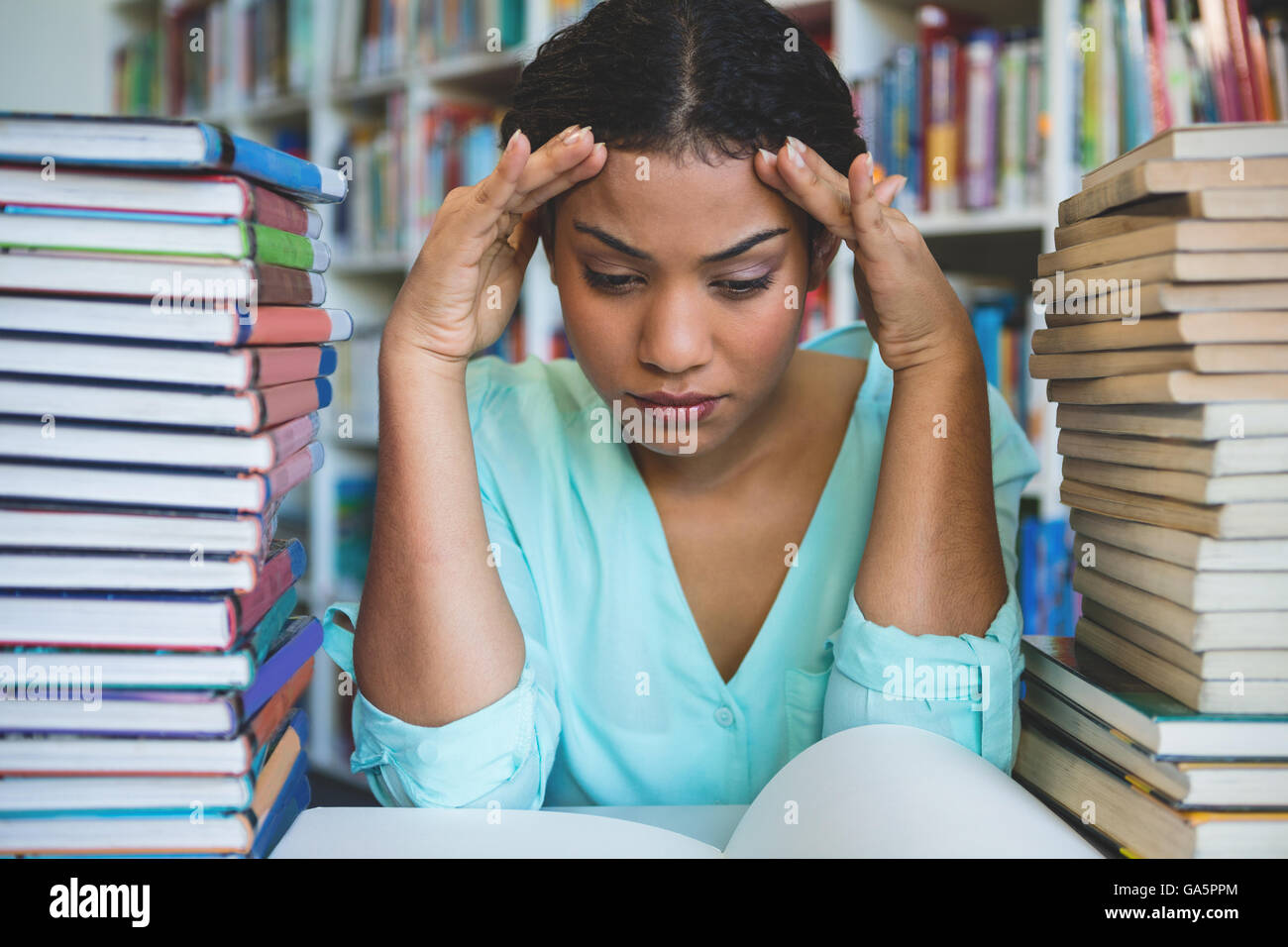 Stressed woman sitting amidst books in library Stock Photo - Alamy