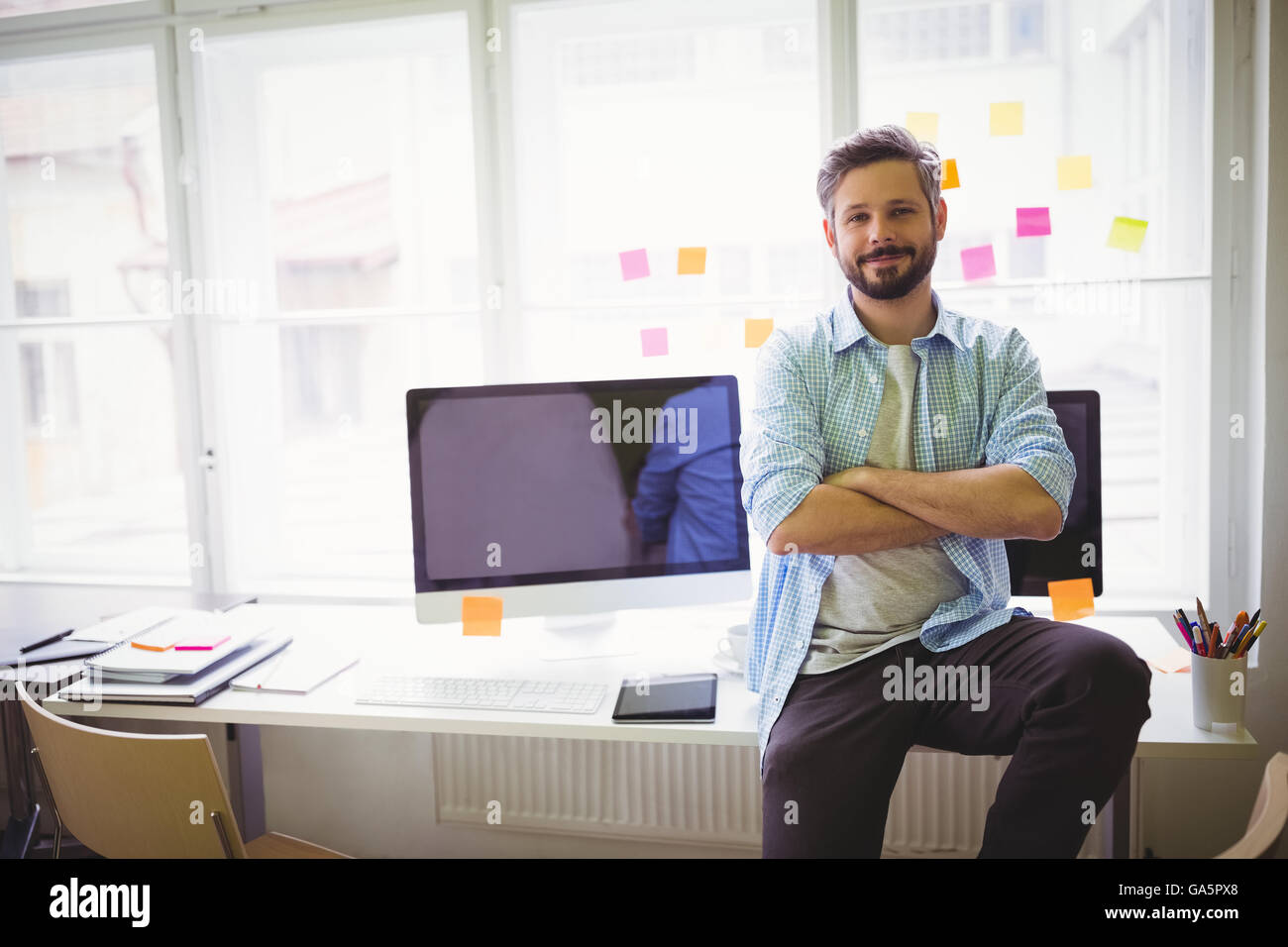 Portrait of businessman sitting on desk in creative office Stock Photo ...