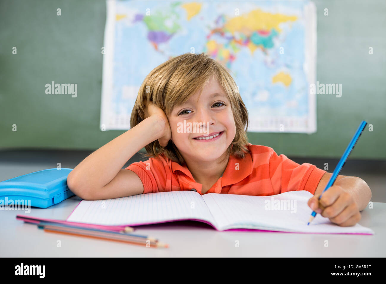 Smiling boy writing on book in classroom at school Stock Photo - Alamy