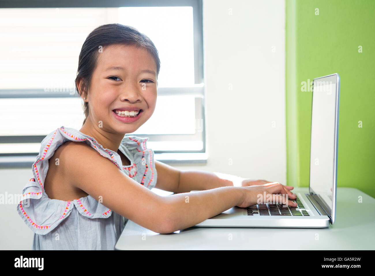 Smiling girl using laptop at table in classroom Stock Photo - Alamy