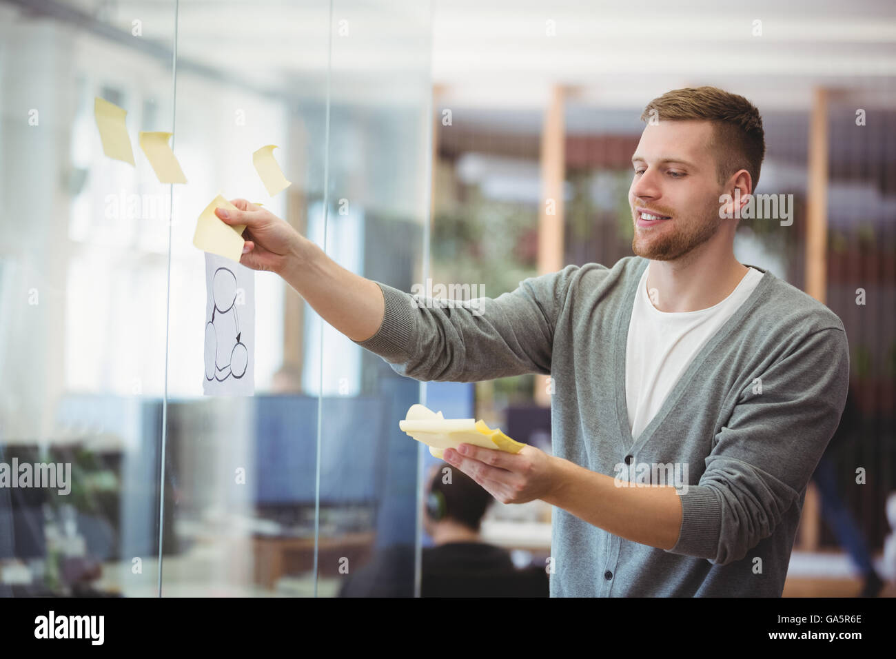 Happy businessman sticking adhesive notes on window in office Stock ...
