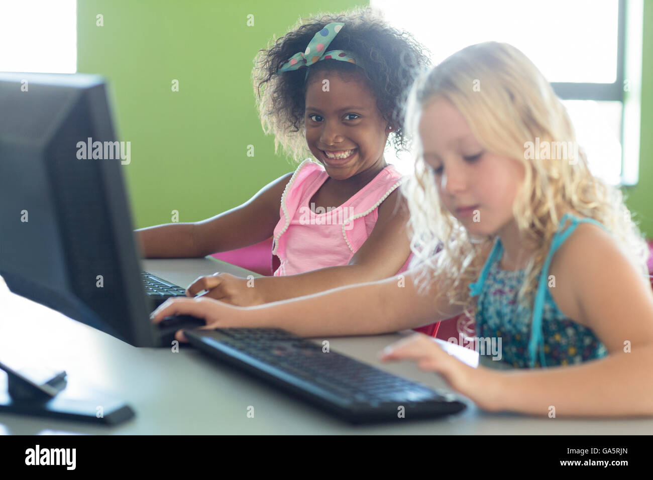 Smiling girl with classmate using computers Stock Photo - Alamy