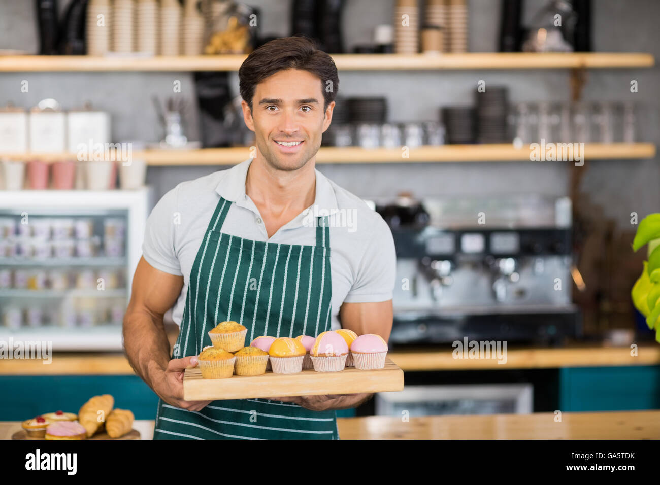 Portrait of smiling waiter holding a tray of cupcakes Stock Photo - Alamy