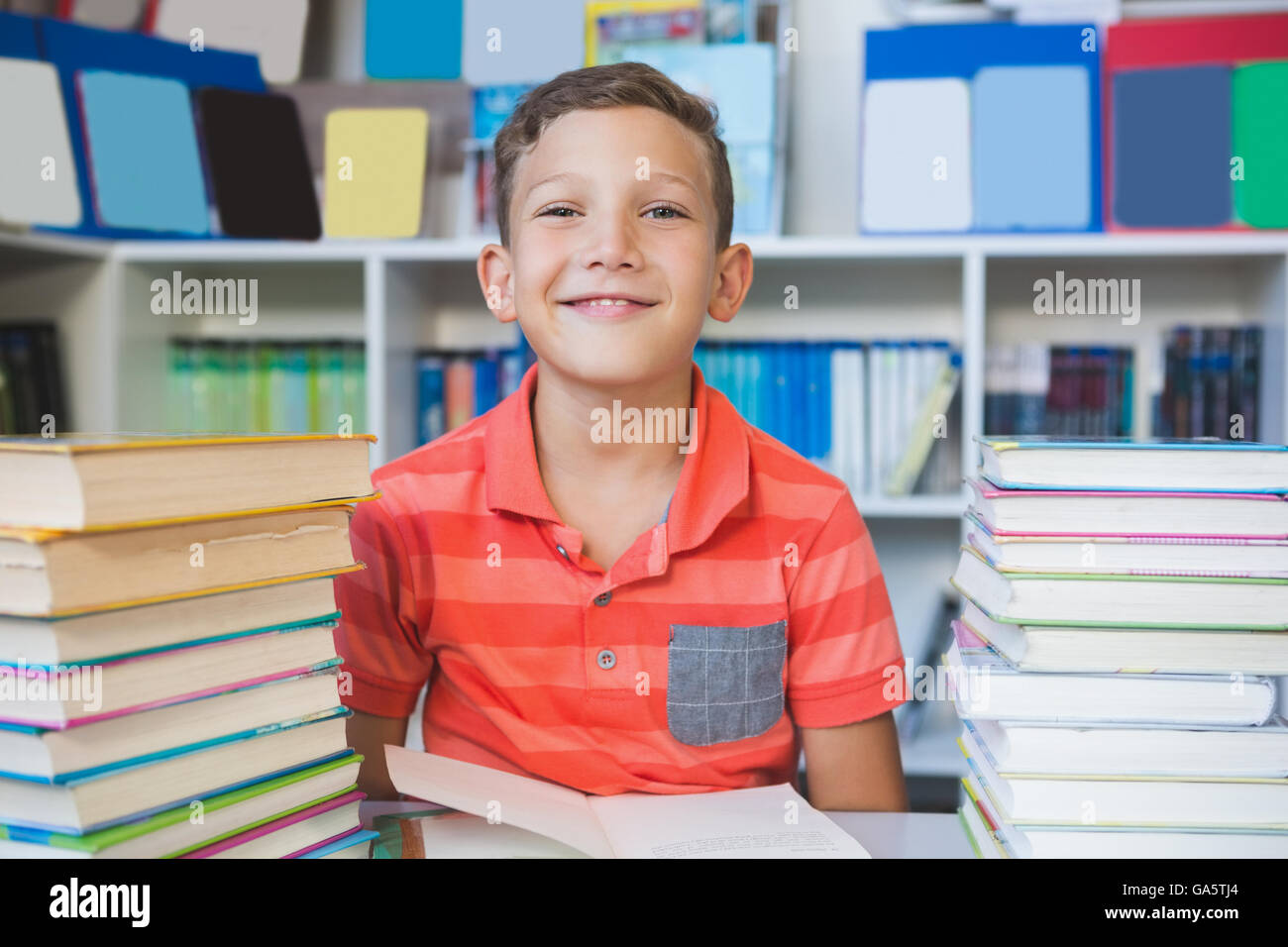 Schoolboy sitting on table and reading book in library Stock Photo - Alamy