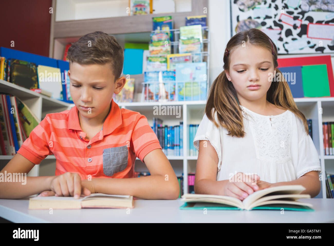Schoolkids reading book in library Stock Photo - Alamy