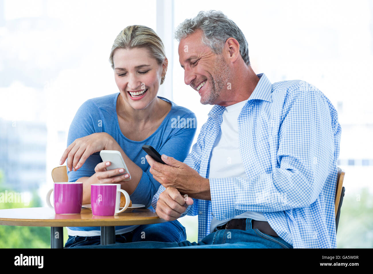 Smiling couple using mobile phones at cafe Stock Photo - Alamy