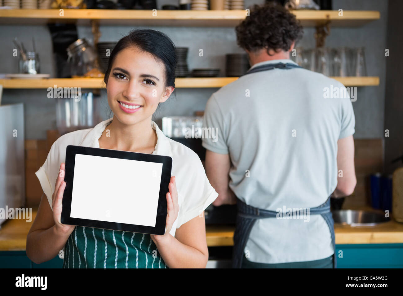 Waitress holding digital tablet while waiter working in background ...