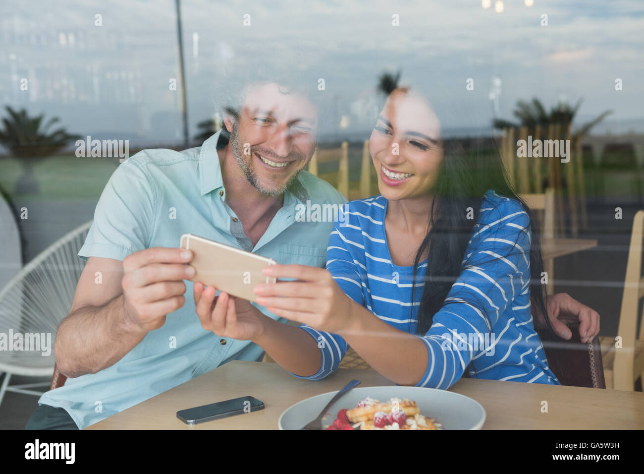 Couple using mobile phone in cafeteria Stock Photo - Alamy