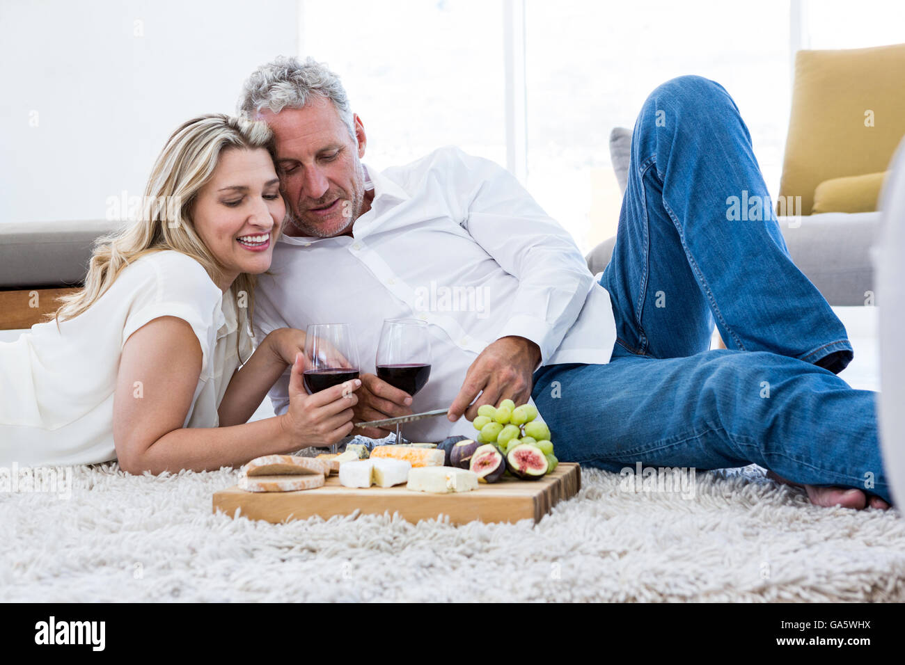 Cheerful couple with red wine and food while lying on rug Stock Photo ...