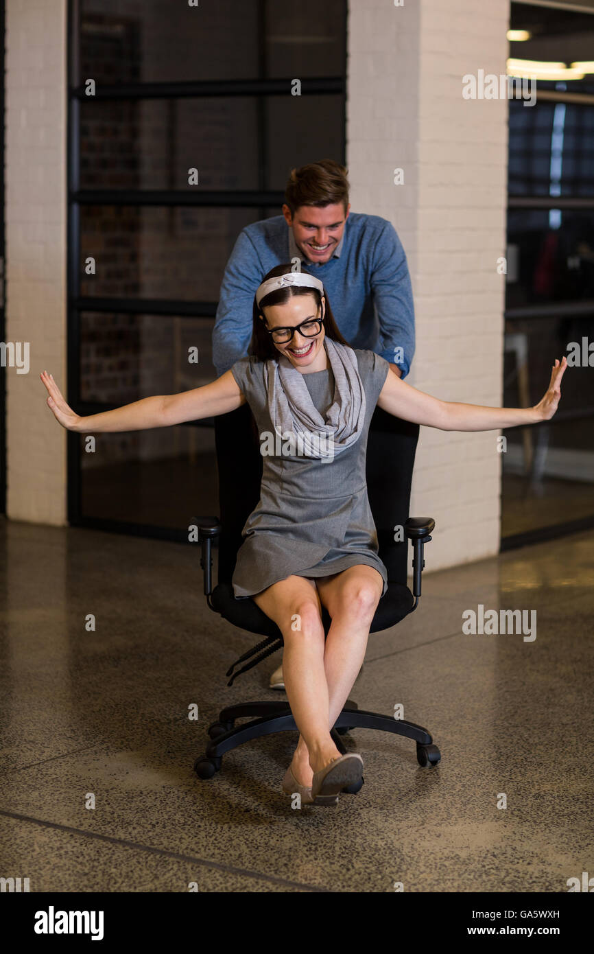Man pushing female colleague sitting on chair Stock Photo - Alamy